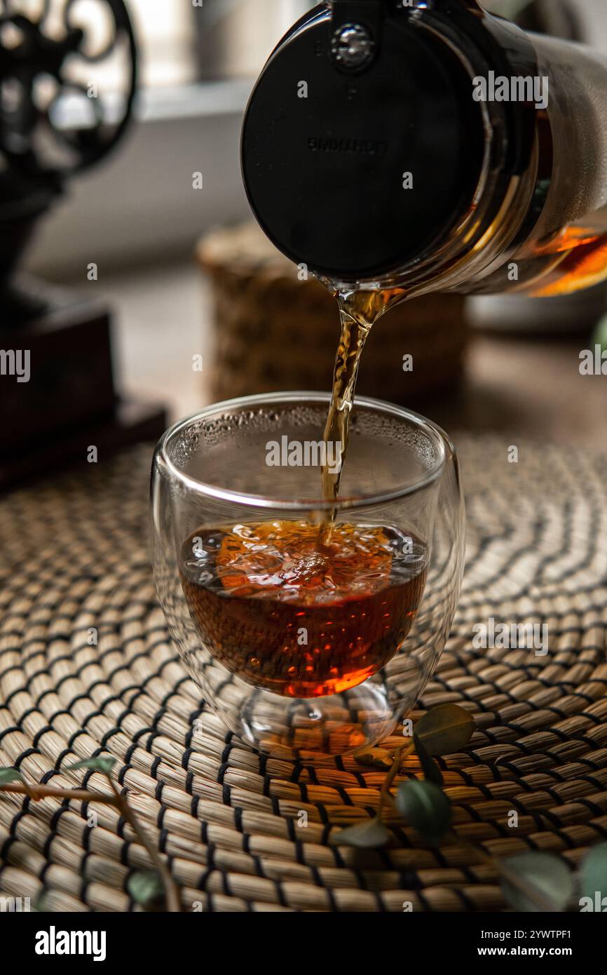 Pouring a beautifully brewed tea into a glass cup placed on a natural ...