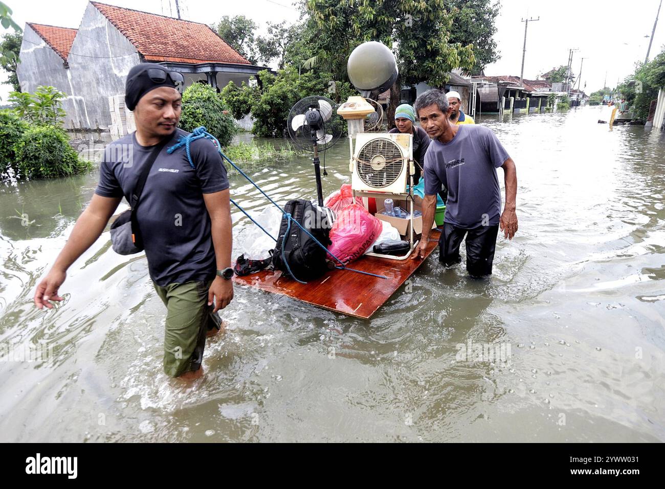 Jombang, Indonesia. 12th Dec, 2024. People wade through flood water with their belongings in ...