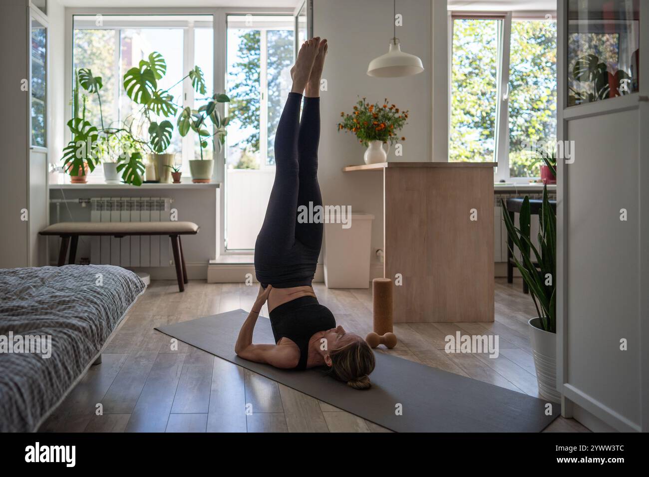 Woman holds shoulder stand pose Sarvangasana, lying on back with legs ...