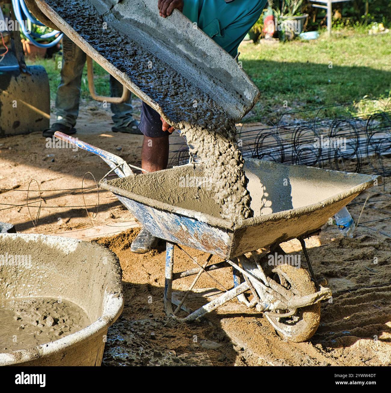 Mixed concrete from a truck is being poured in an old wheelbarrow at a ...