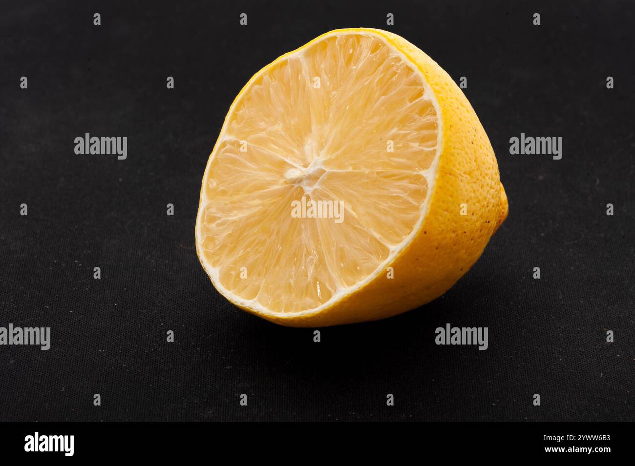 A lemon is cut in half and is sitting on a black surface. The lemon is ...