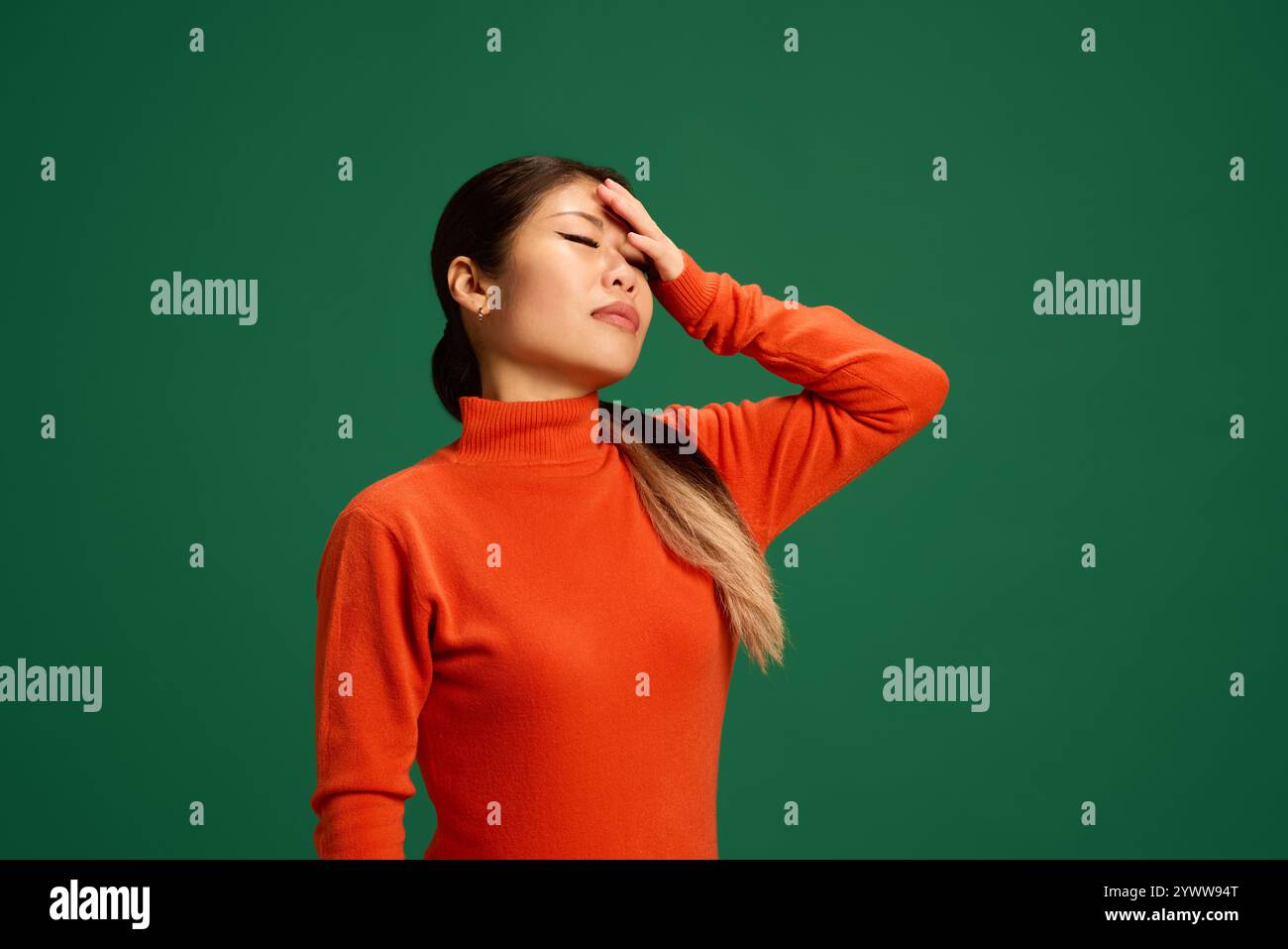 Young Asian woman feeling bad holding hands on head against green ...
