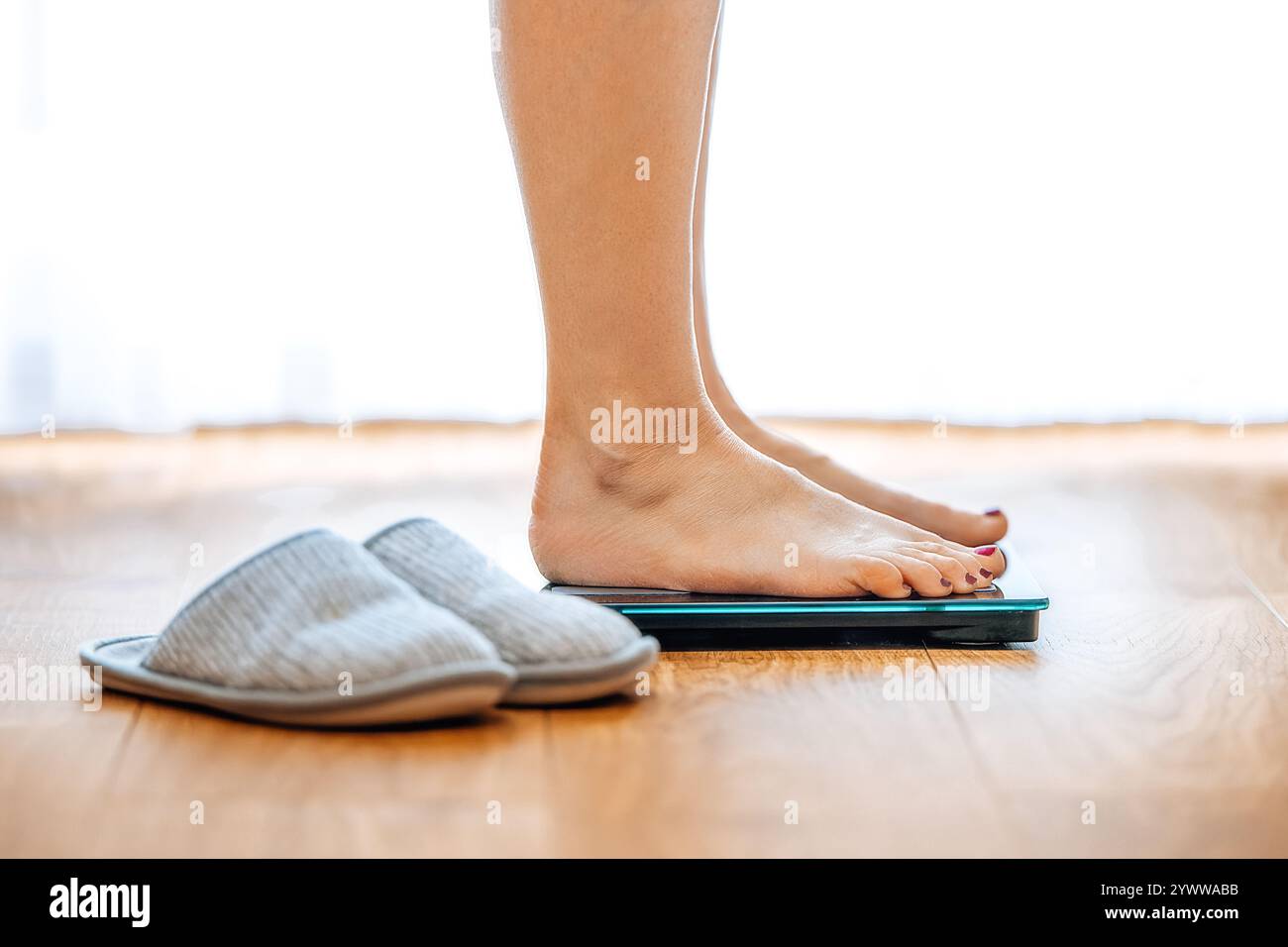 Woman stands on scale and weighs herself in the morning in the living ...