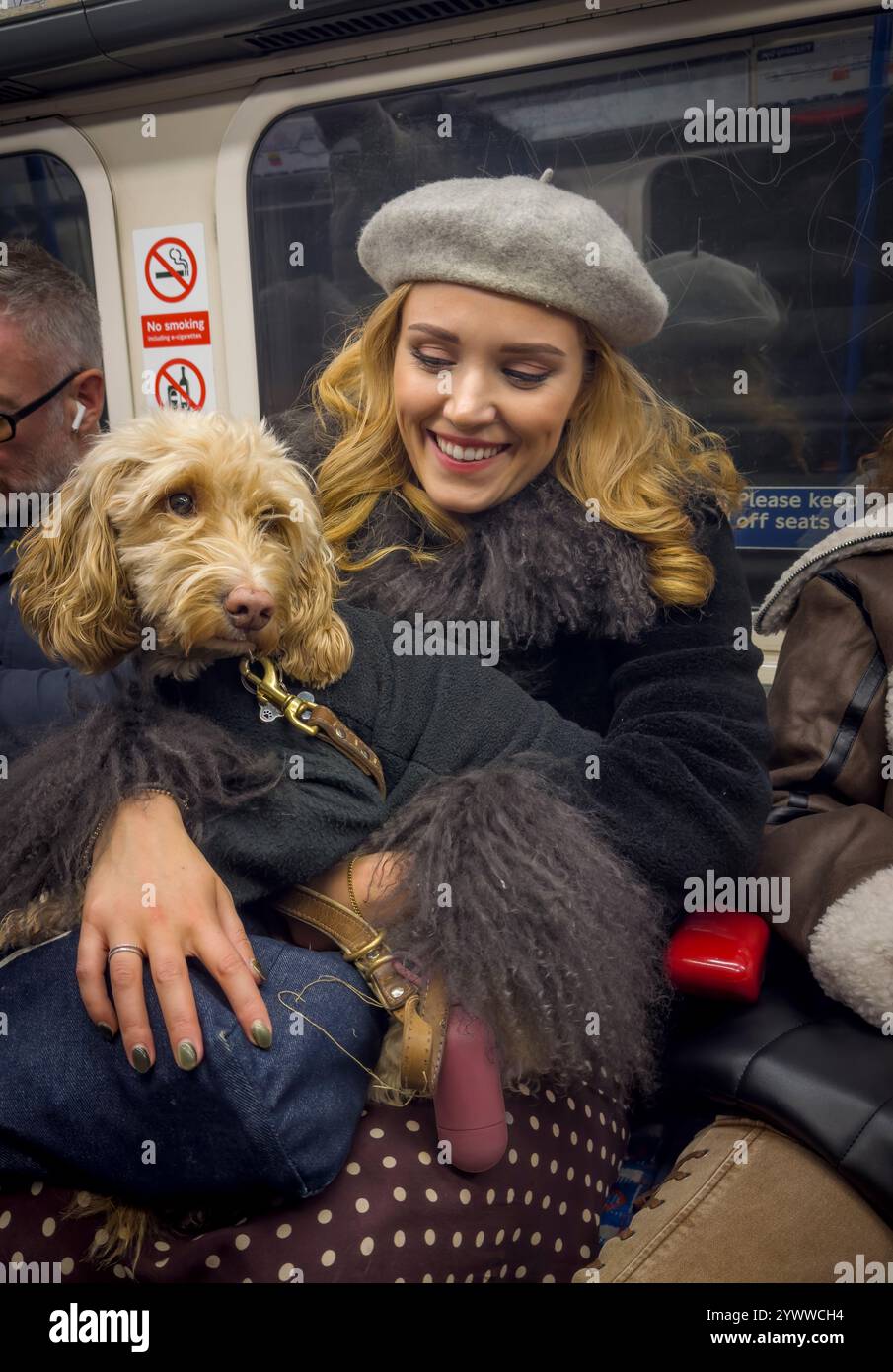 A woman is seated on a tube train in London, UK, smiling while holding ...
