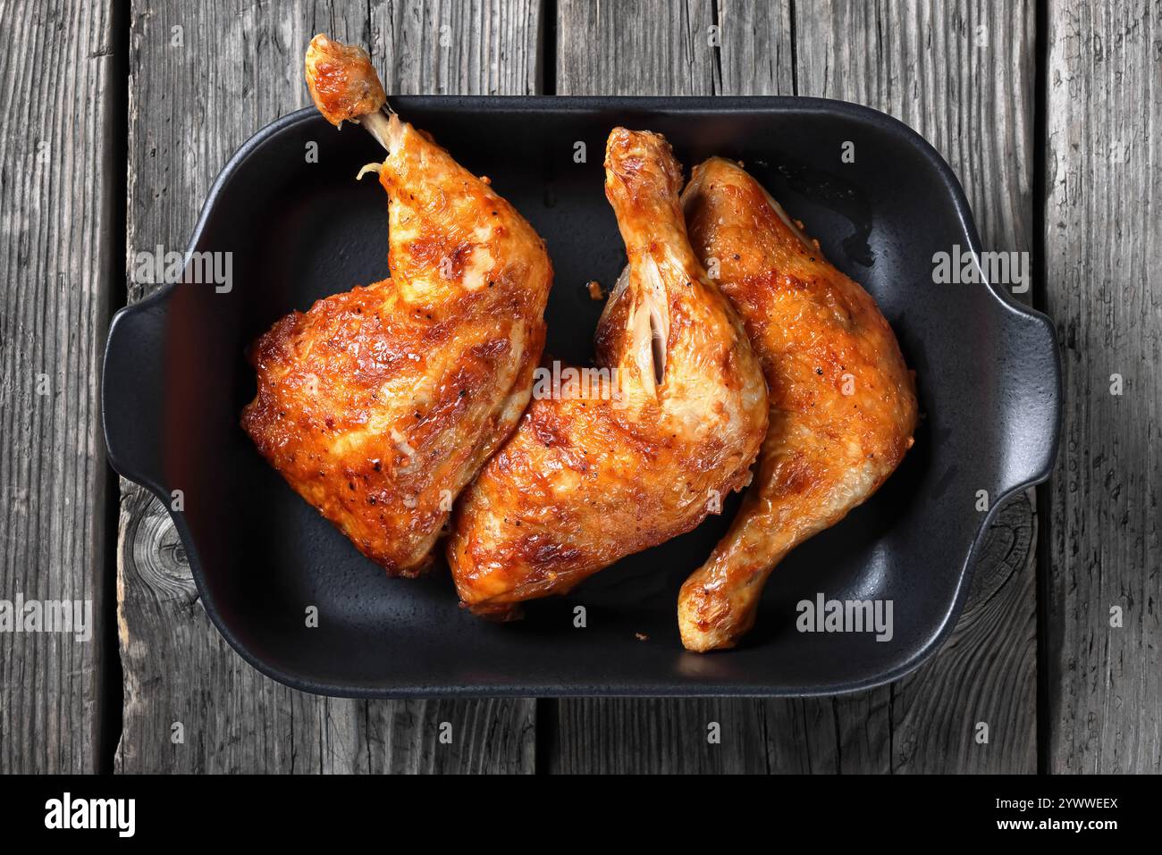 baked in oven three chicken leg quarters in black baking dish on grey ...