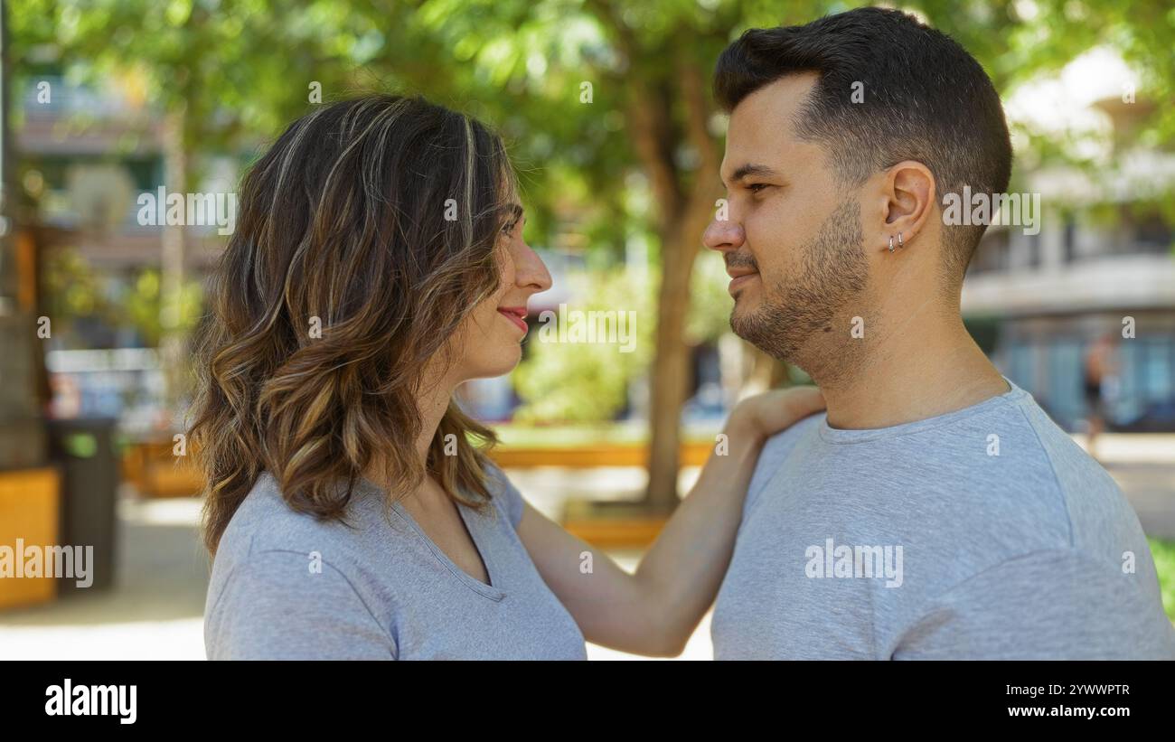 Couple gazing at each other in a sunny urban park, both with casual ...