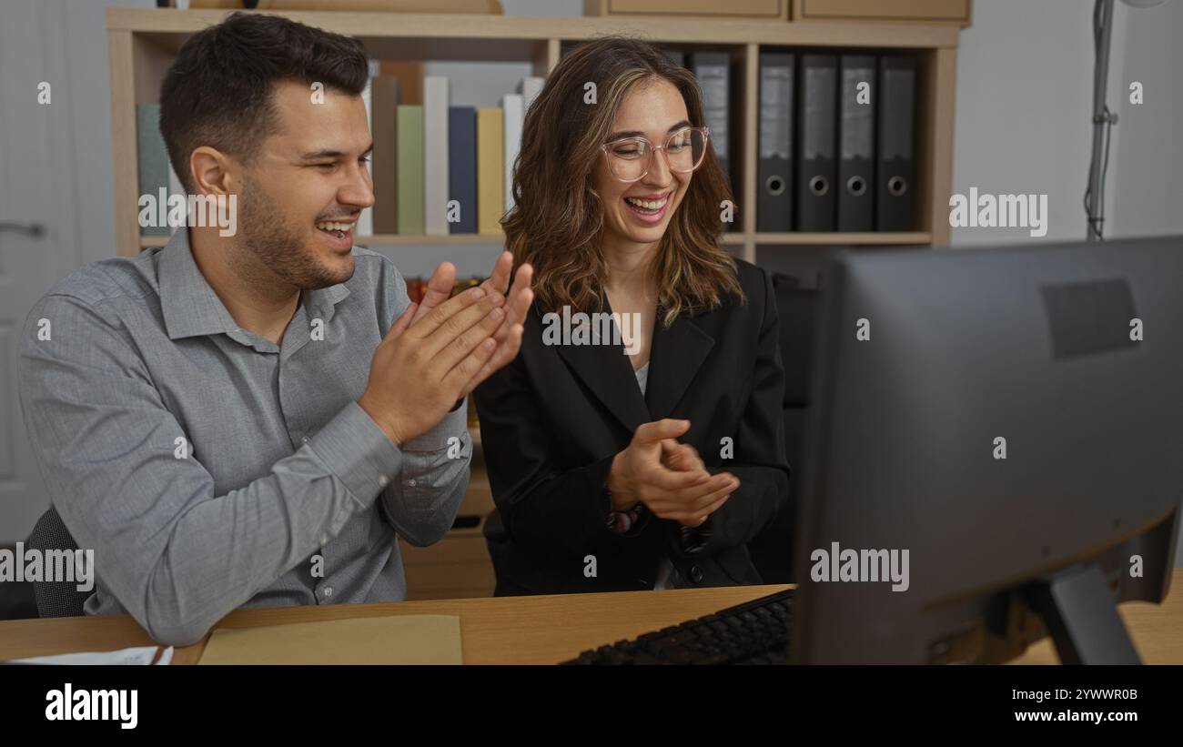 Man and woman in an office clapping while looking at a computer monitor ...