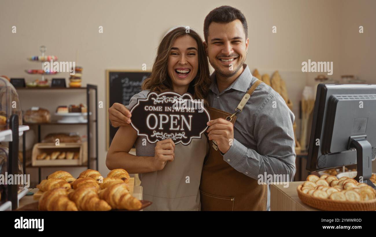 Two smiling bakers, a woman and man, holding an open sign in a cozy ...