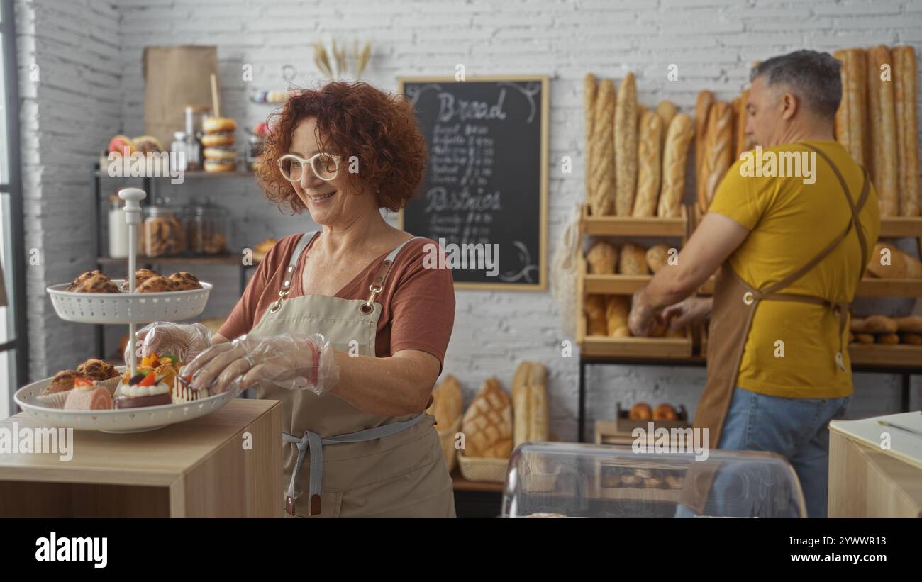 Woman and man working together in a bakery arranging pastries and bread ...