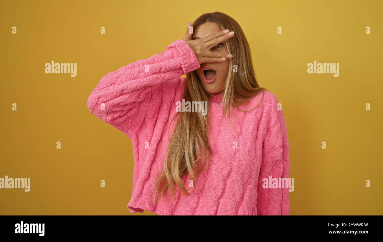 Woman posing playfully with hand over face in pink sweater against ...