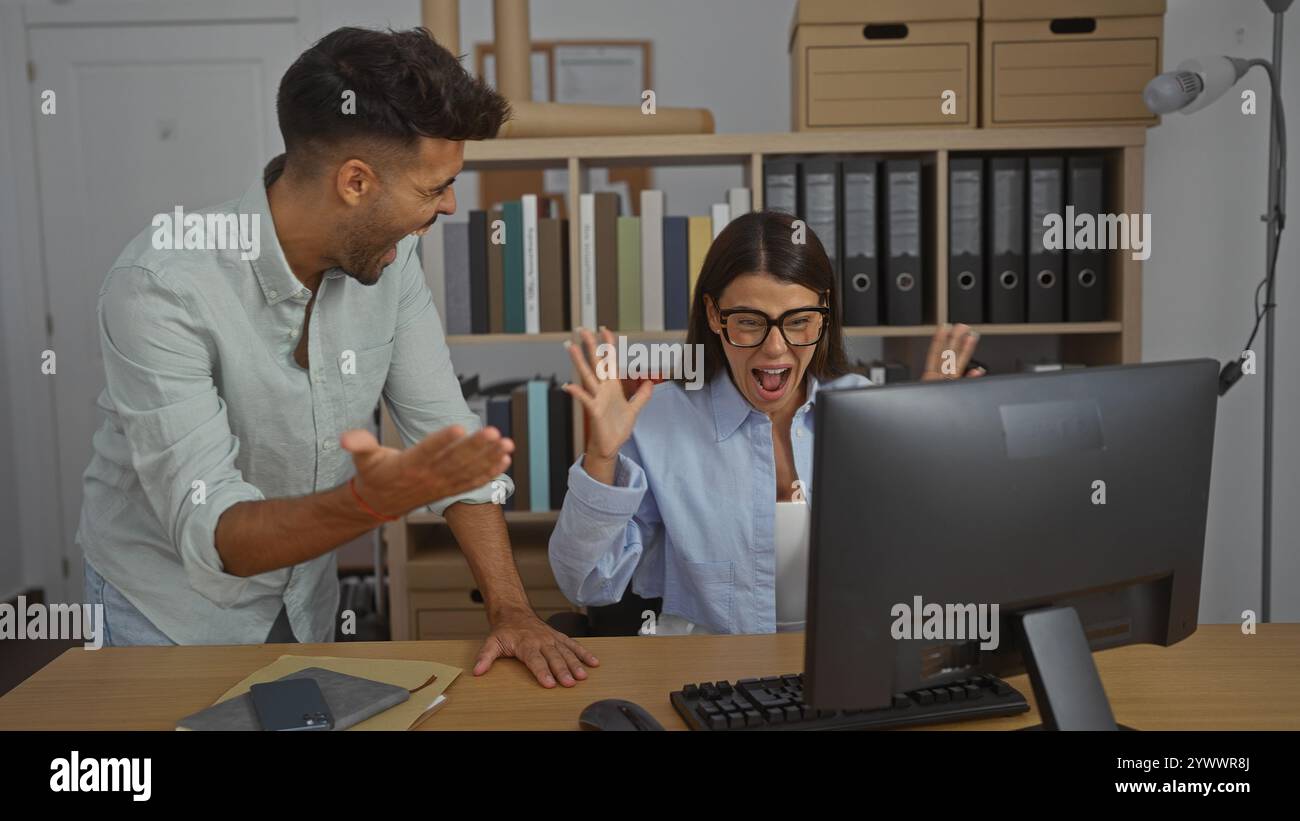 Man and woman celebrating success at computer screen in modern office ...