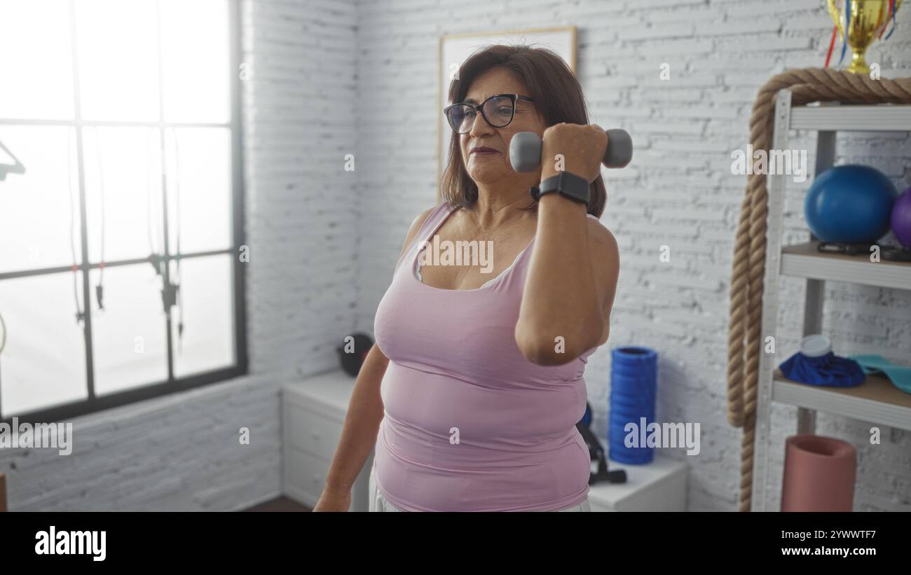 Middle-aged hispanic woman lifting dumbbell in a gym setting, wearing ...
