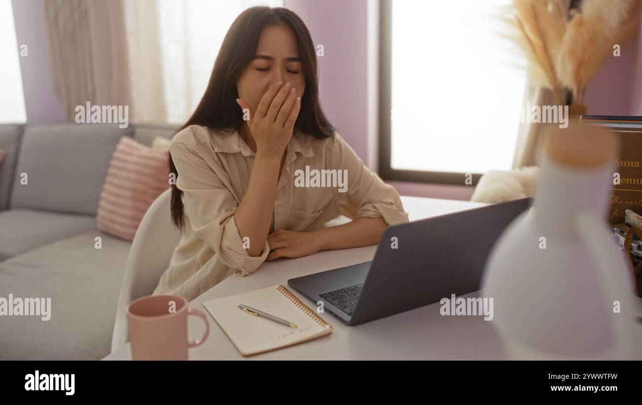 Young chinese woman yawning indoors in her living room with a laptop ...