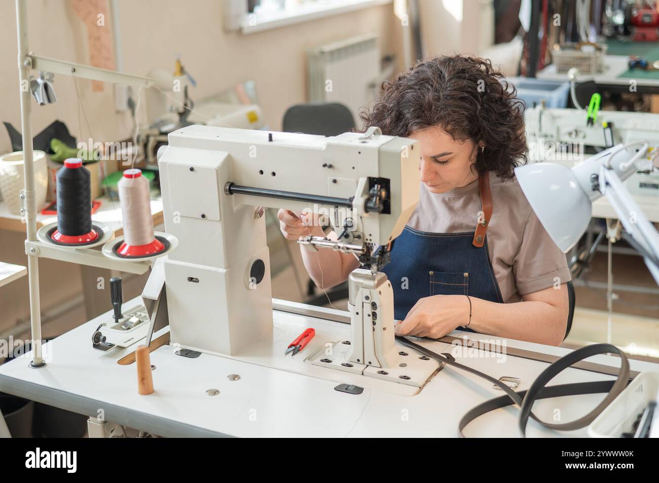 A woman tanner sews a leather belt on a sewing machine Stock Photo - Alamy