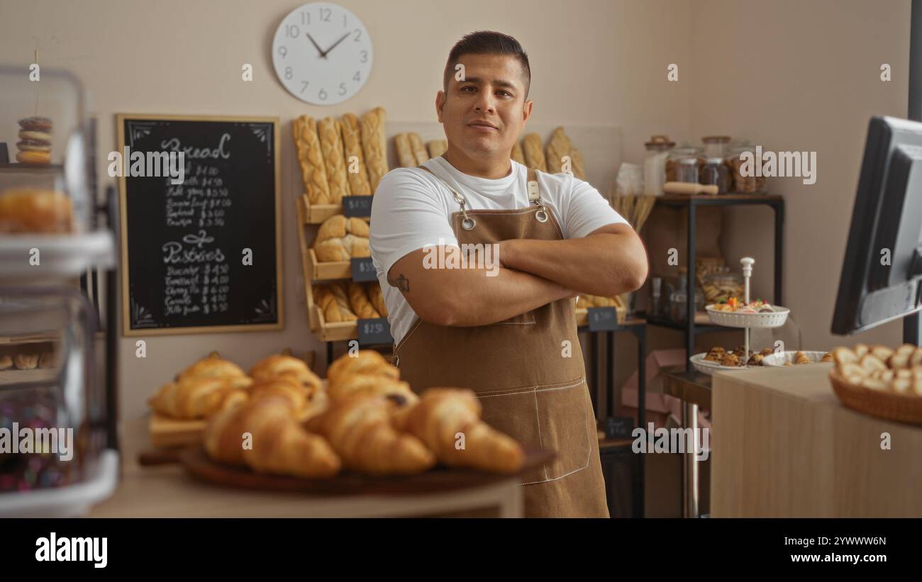 Young hispanic man with arms crossed in a bakery shop, wearing an apron ...