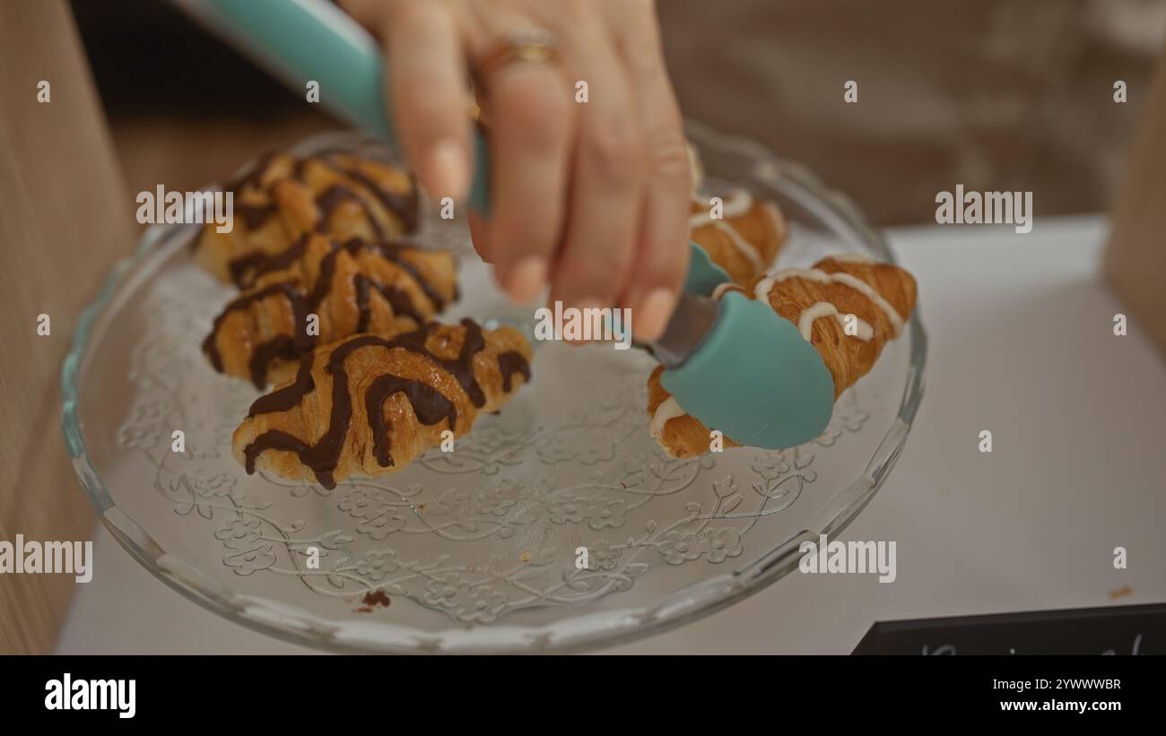 Woman selecting croissants with tongs in a bakery shop with a glass ...