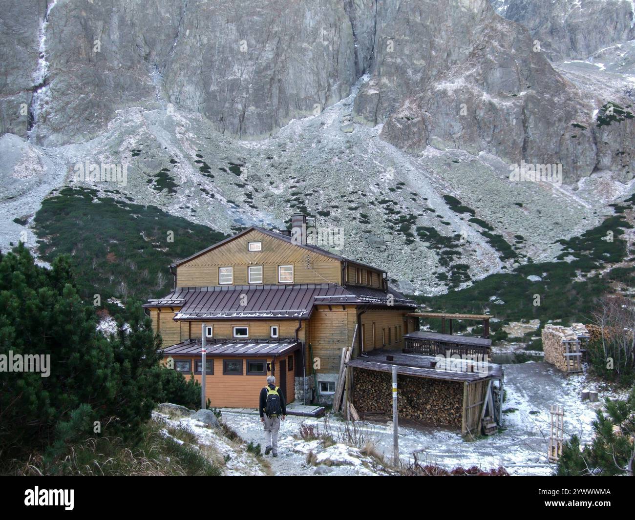 Man walking to snowy mountain lodge with cliffs behind in High Tatras ...