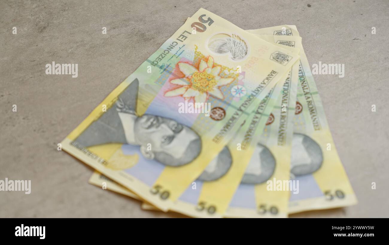Romanian banknotes scattered on a concrete surface, highlighting 50 leu ...