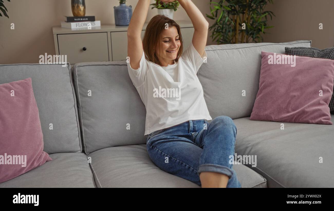 A beautiful young woman relaxes on a stylish couch in her cozy living ...