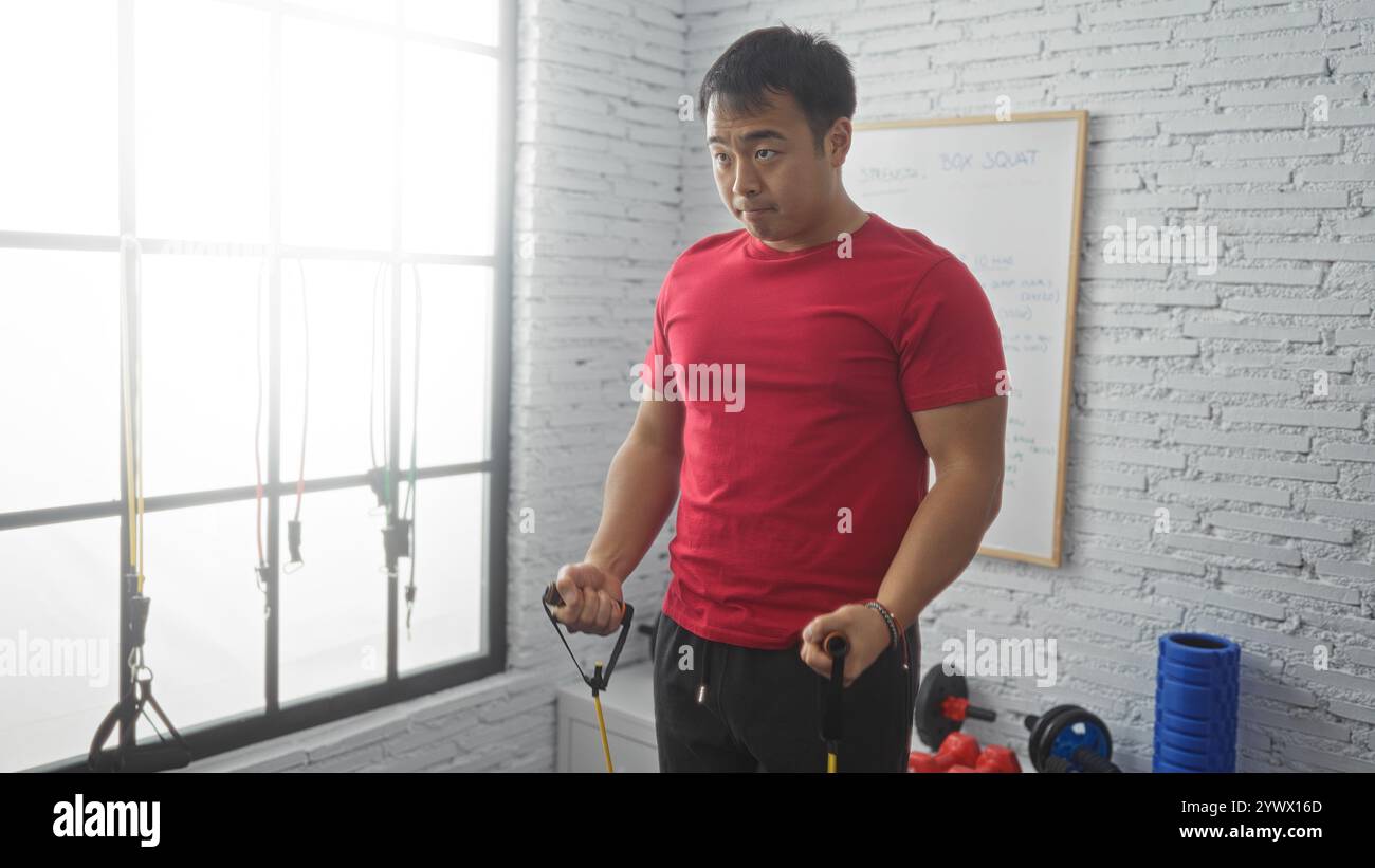 Young chinese man exercising indoors at a gym, surrounded by equipment ...