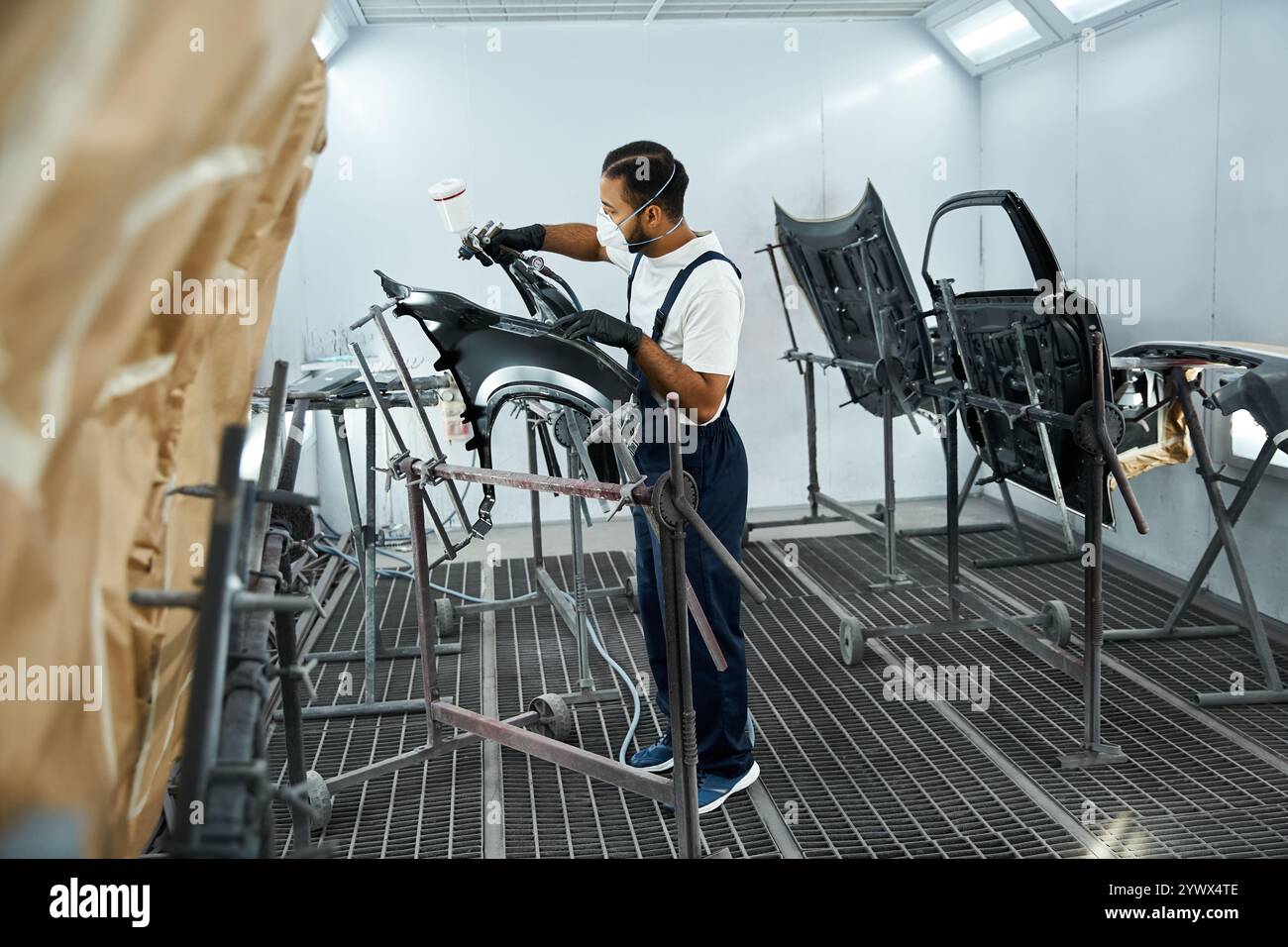 A handsome mechanic focuses on repairing car parts in a well lit garage ...