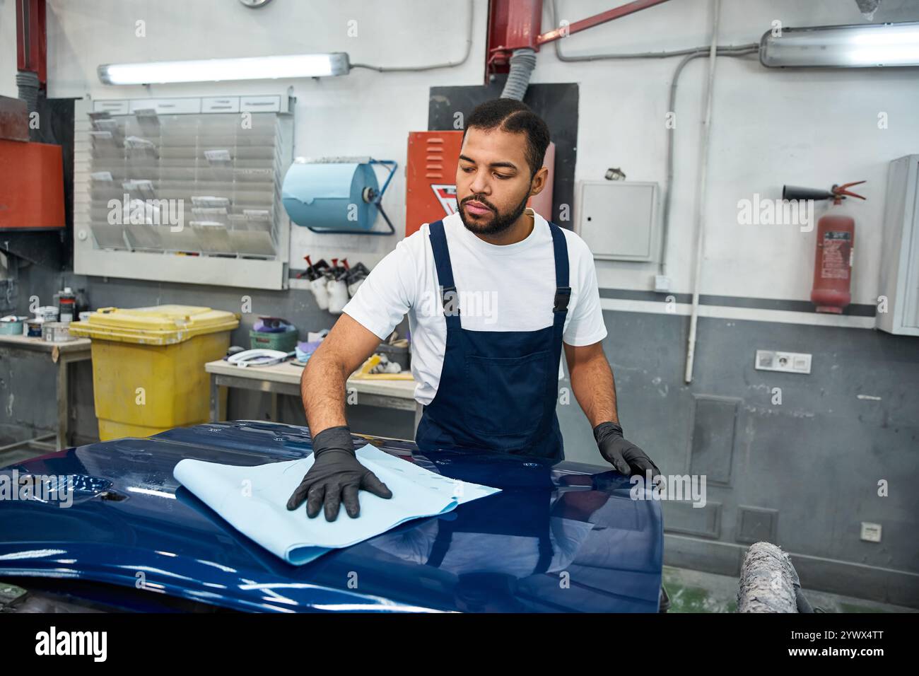 A handsome mechanic works on a blue car part in a tool filled workshop ...