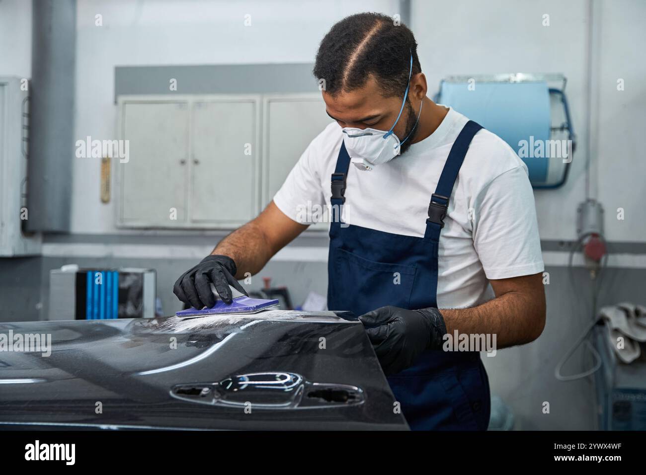 A handsome young mechanic is focused on restoring a vehicles surface ...