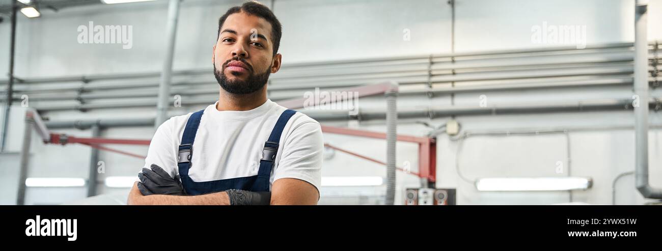 A handsome young mechanic stands proudly with arms crossed in an ...