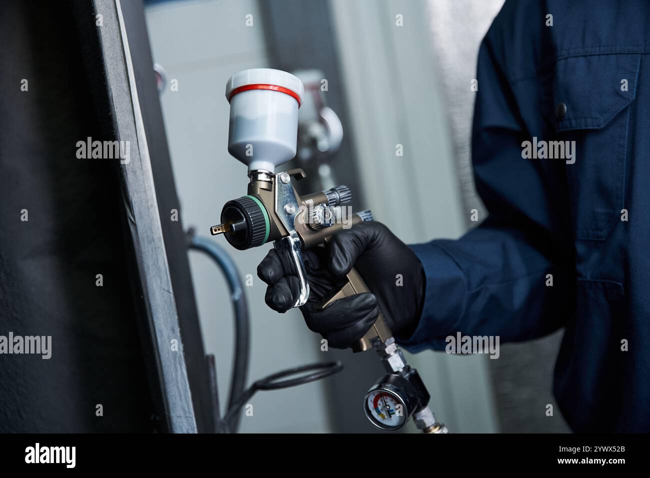 A skilled young mechanic applies paint using a spray gun while working ...