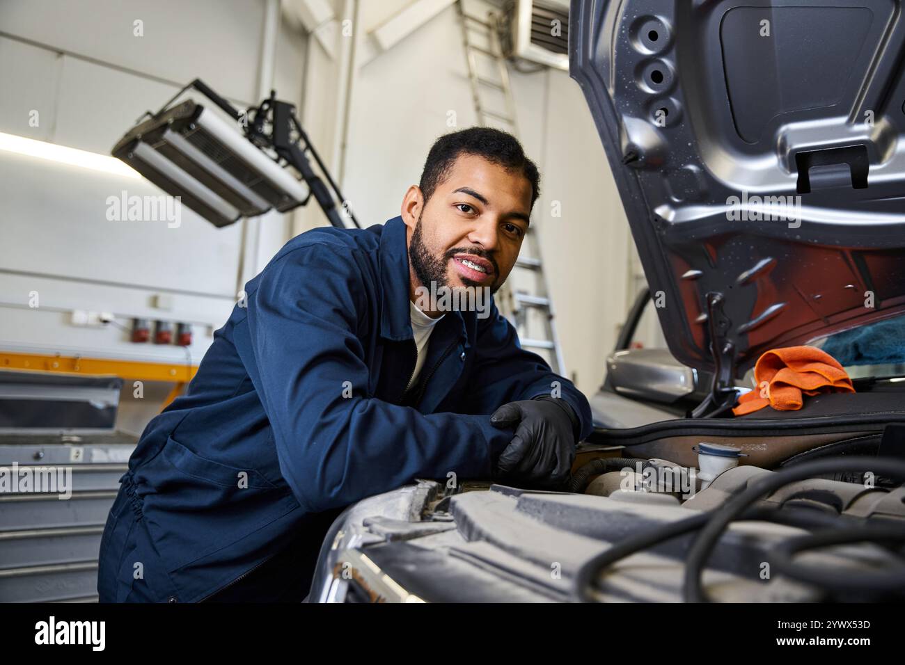A skilled young mechanic smiles while inspecting an engine under a ...