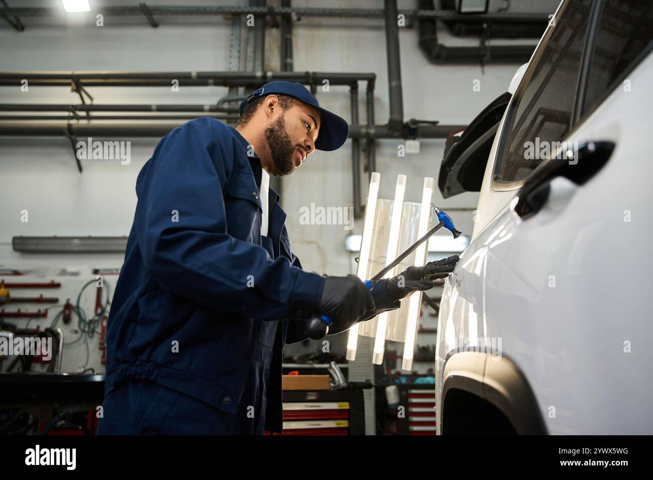 Handsome mechanic focuses intently on fixing a vehicle in a busy ...