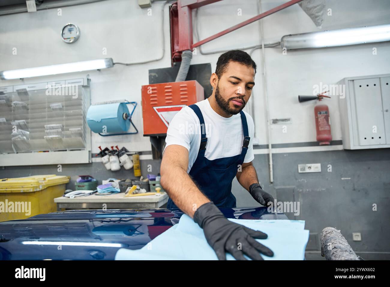 Passionate young mechanic works hard to restore a cars shine in a busy ...