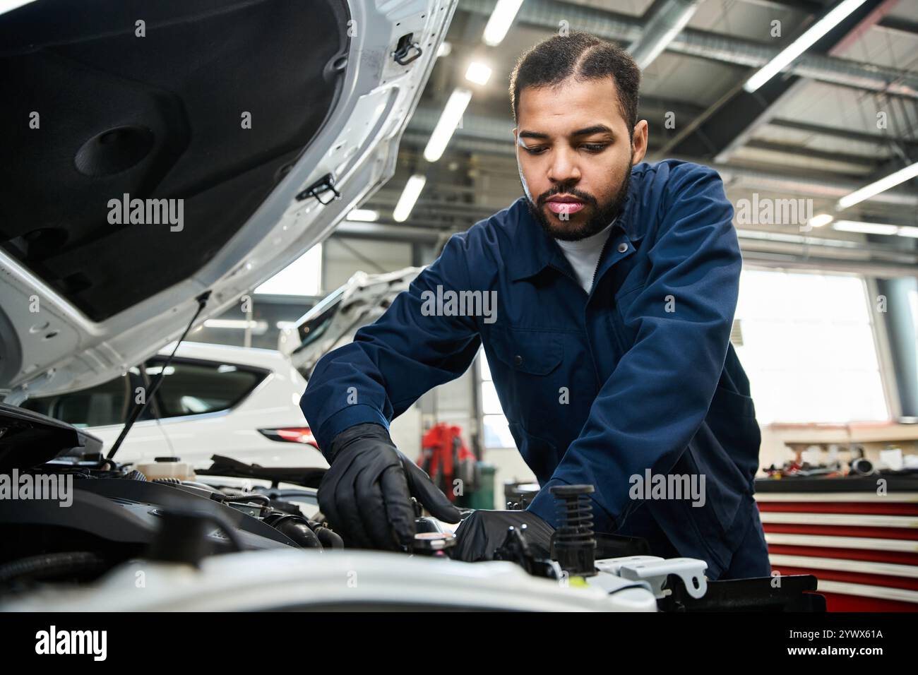 Handsome young mechanic works diligently under the hood of a vehicle in ...