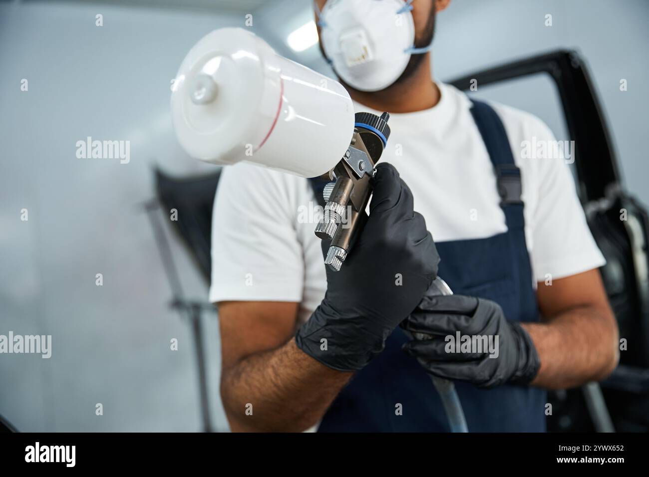 Skilled mechanic focuses intently while using a spray gun for auto body ...