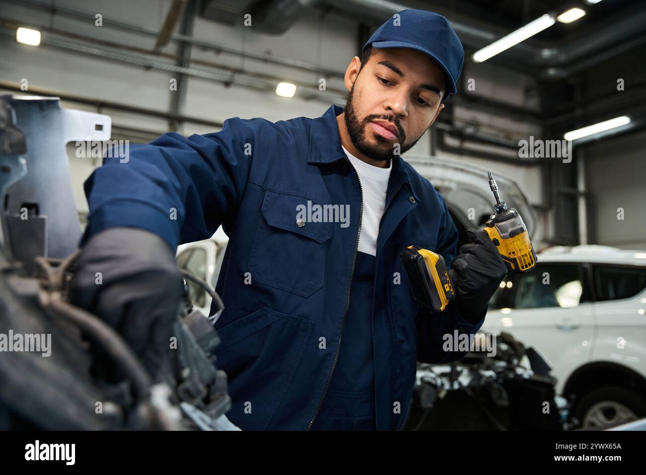 Young mechanic focuses intently on repairing a vehicle engine with ...