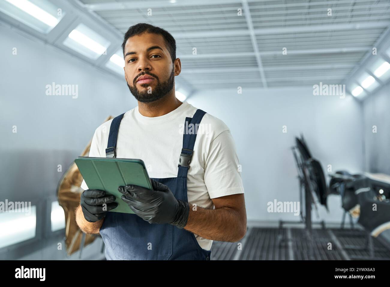 A confident mechanic stands in a bright workshop, ready to work with a ...