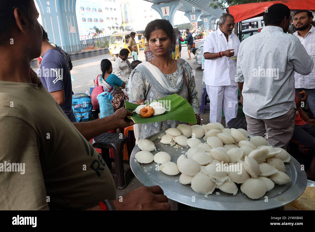 Food vendor serving idli and vada pav to a customer at a street stall ...