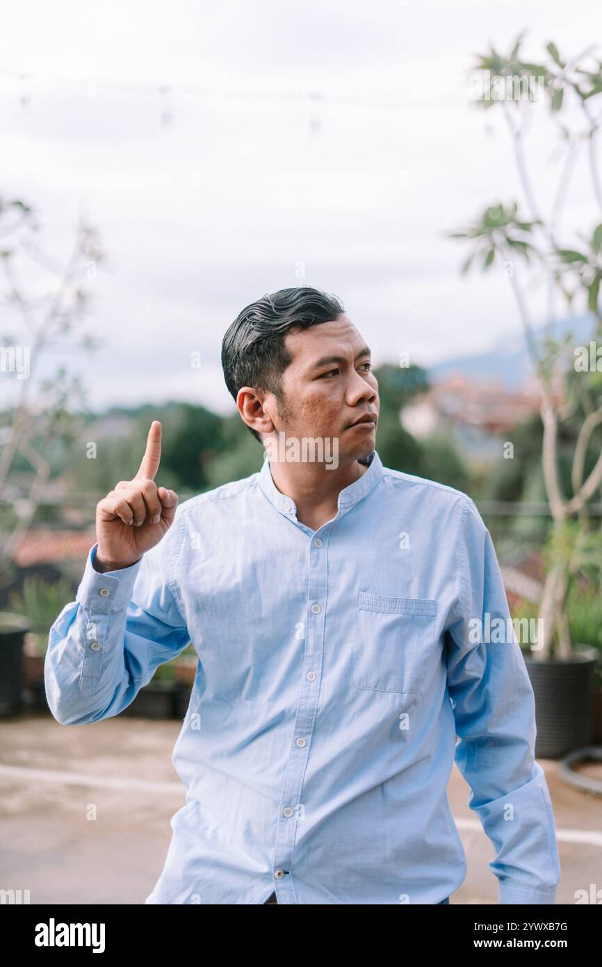 A Southeast Asian man pointing upwards with one finger, conveying ...
