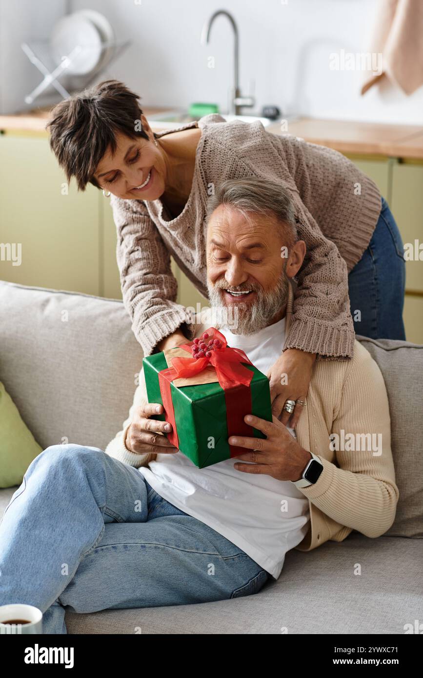 A woman surprises her partner with a wrapped gift while they relax on ...