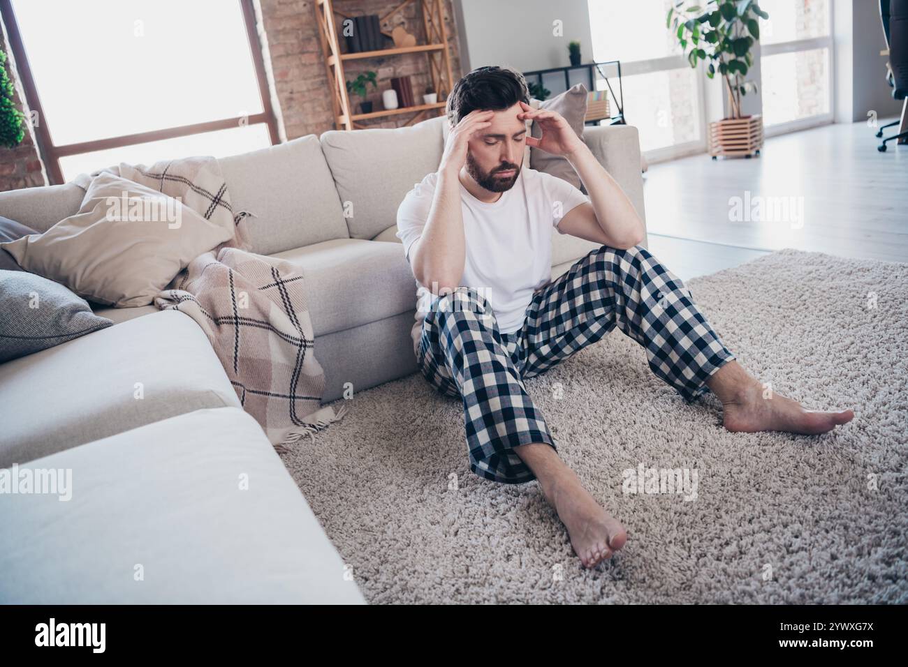 Photo of sad upset moody gloomy man wearing pajama sitting on carpet ...