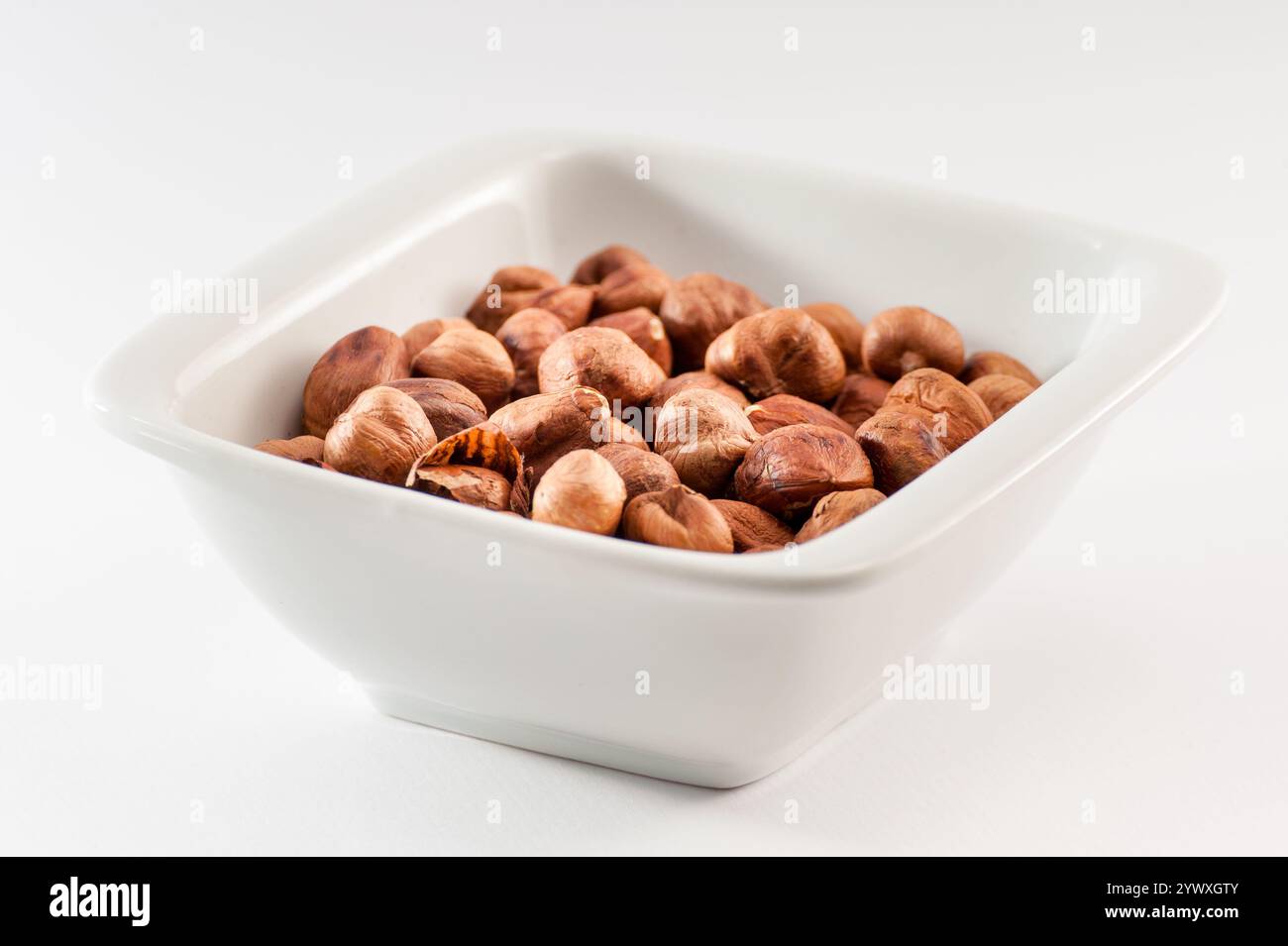 Pile of fried hazelnuts in a white ceramic bowl isolated on a white ...