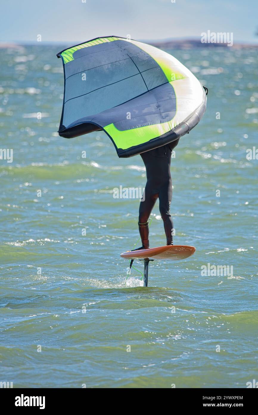 Man is wing foiling using handheld inflatable wing and hydrofoil ...