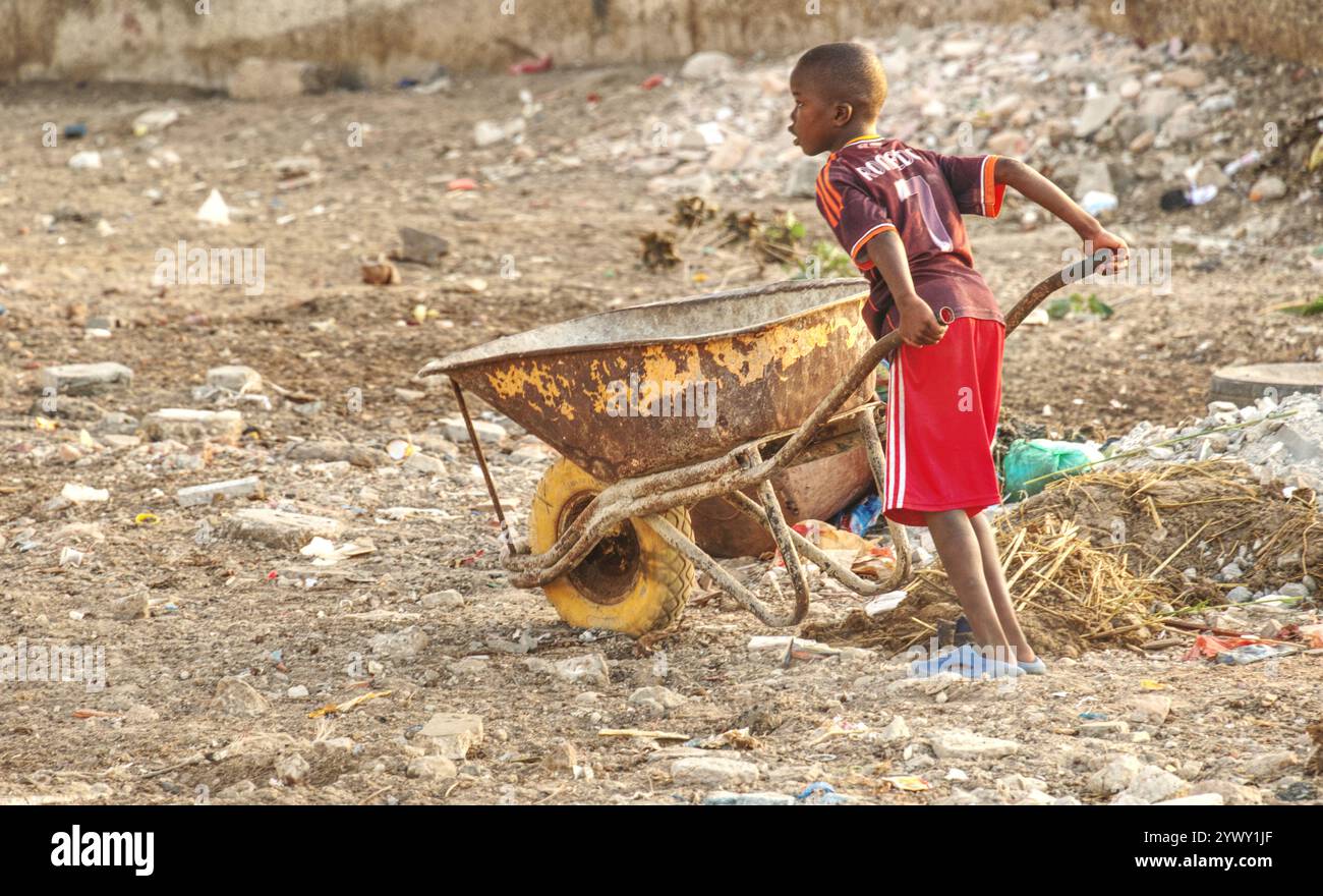 A young boy is doing some garbage collection work with his wheelbarrow ...