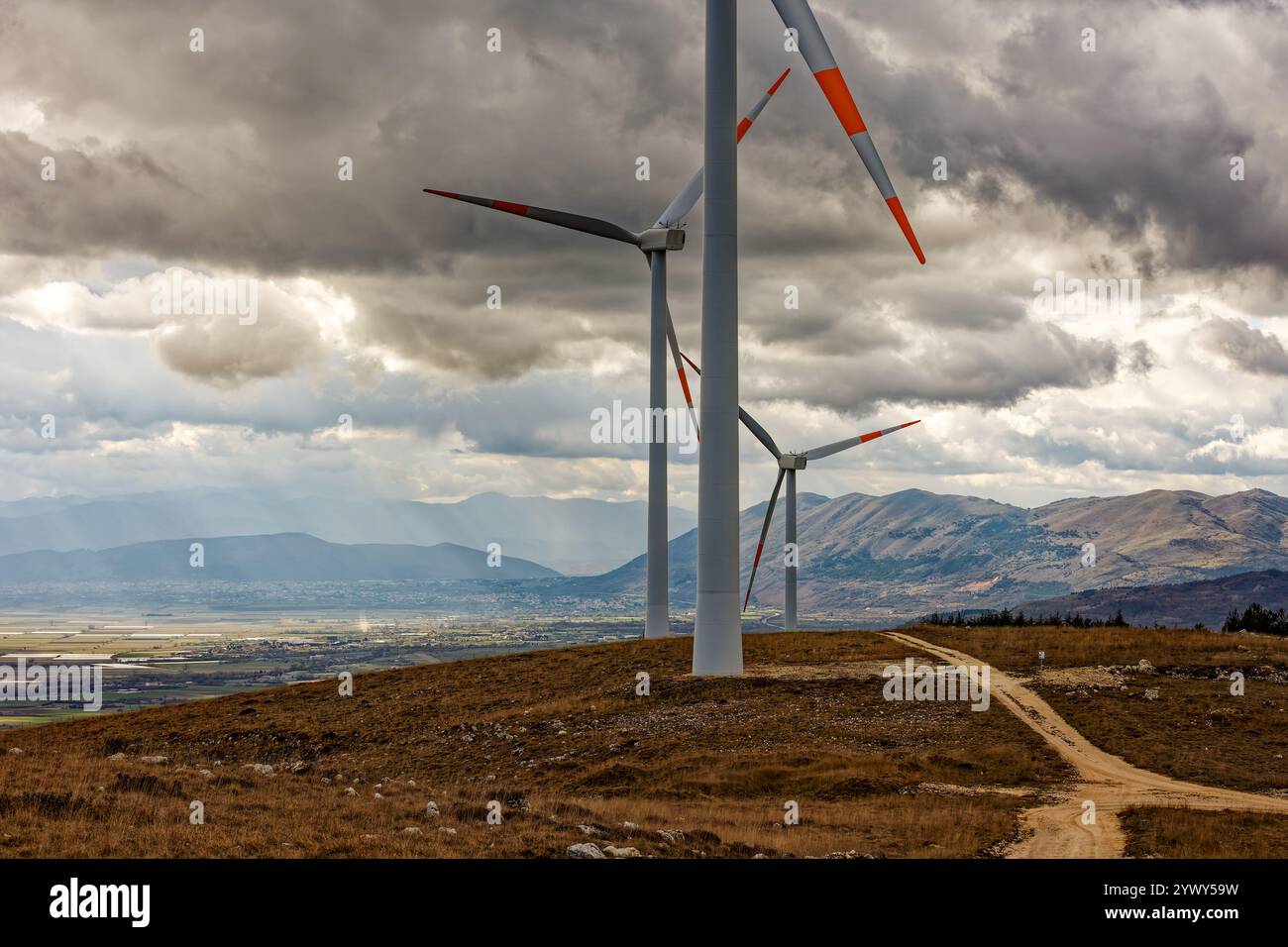 Wind turbines on a hilltop during sunset with dramatic clouds and sun ...