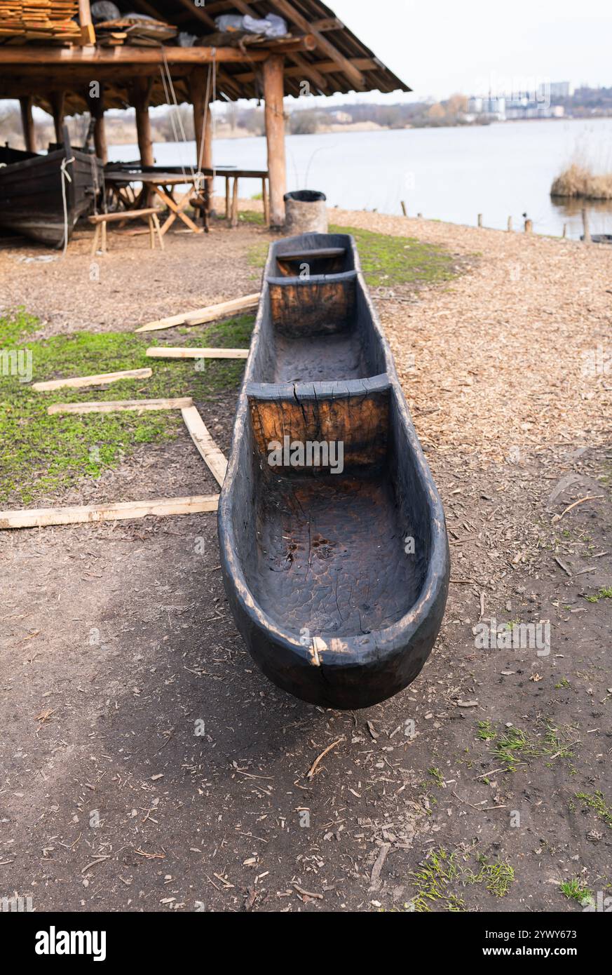 A handcrafted dugout canoe displayed near a lakeside workshop ...