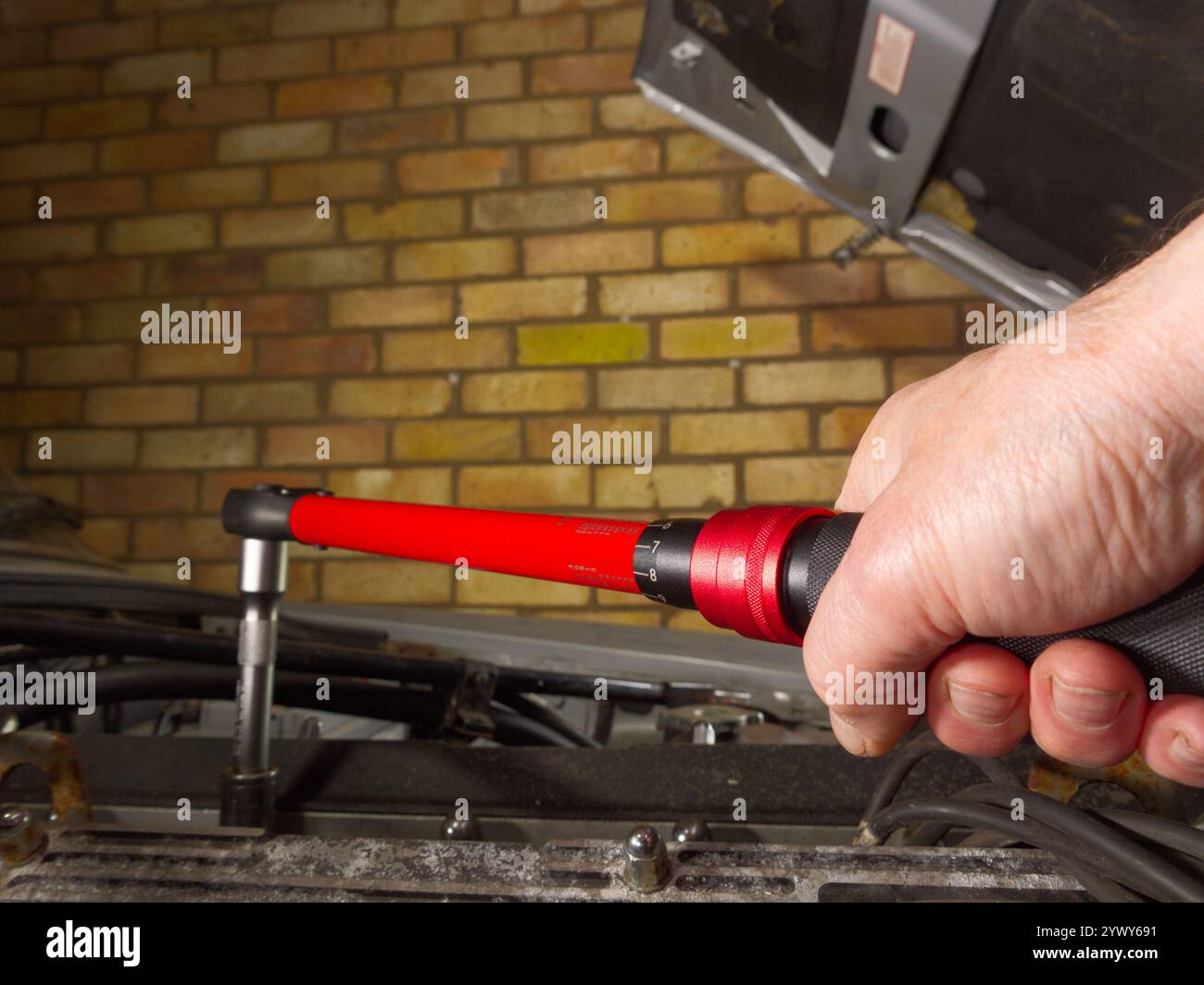 Closeup of a man’s hand in the engine bay of a car in a garage, turning ...