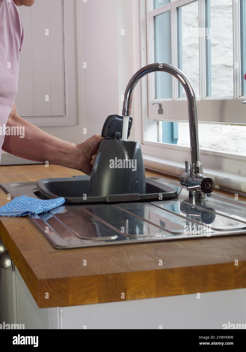 Closeup of a senior man’s hand holding a kettle under running water ...