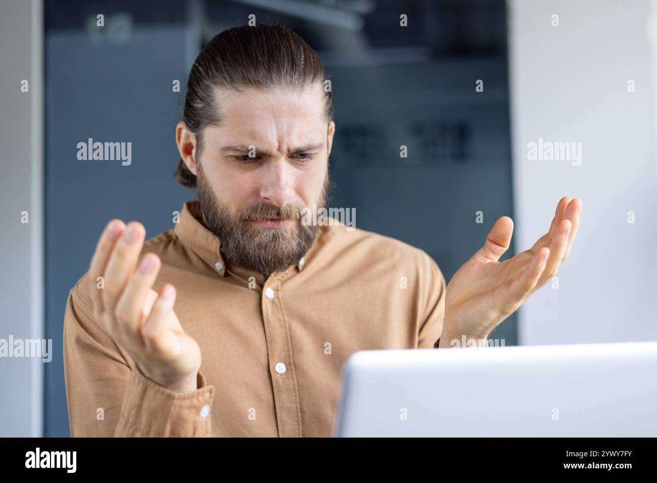 A man looks perplexed as he gestures toward his laptop, reflecting ...