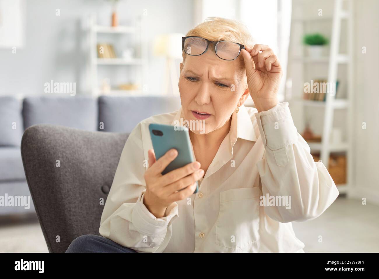 Shocked in worry, concerned mature woman in glasses holding smartphone ...