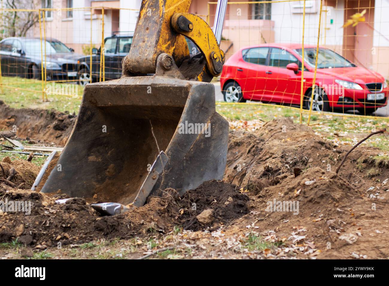 A bright yellow excavator is actively digging a sizable hole deep into ...